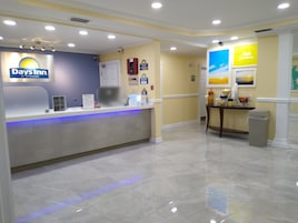 Uma área de recepção com a placa Days Inn, um balcão de atendimento, uma lixeira e uma pequena mesa com dispensador de bebidas.