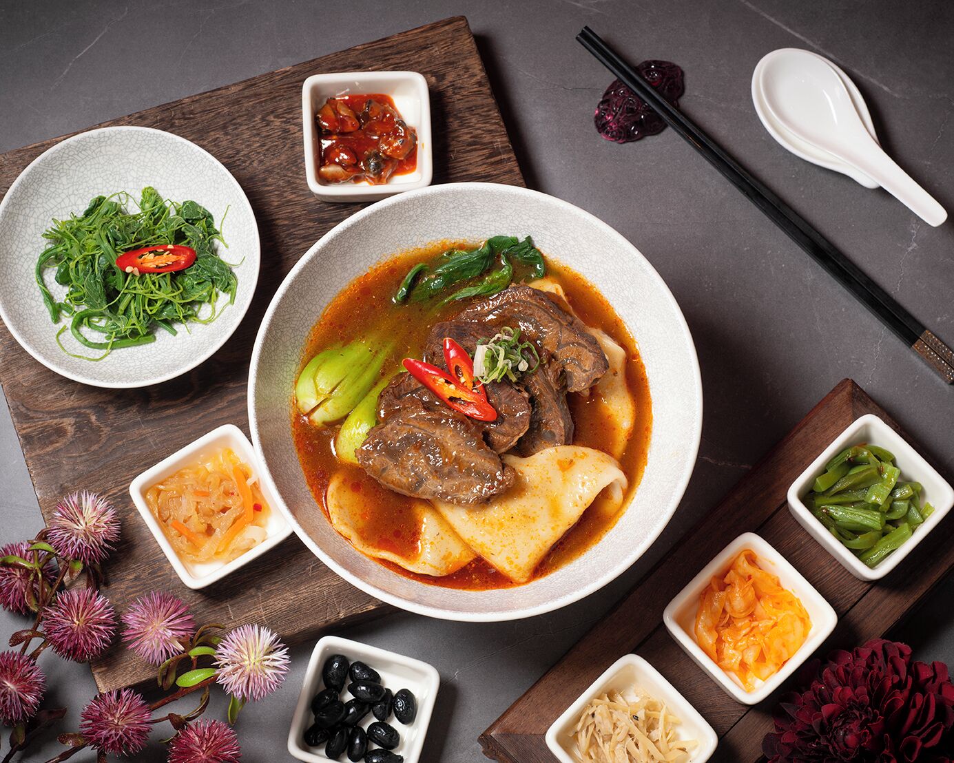 Uma tigela de ensopado de carne com legumes, rodeada por acompanhamentos e condimentos diversos.