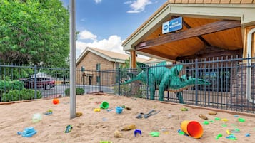 Uma área de recreação infantil com areia, brinquedos e uma placa que diz 'Best Western'.