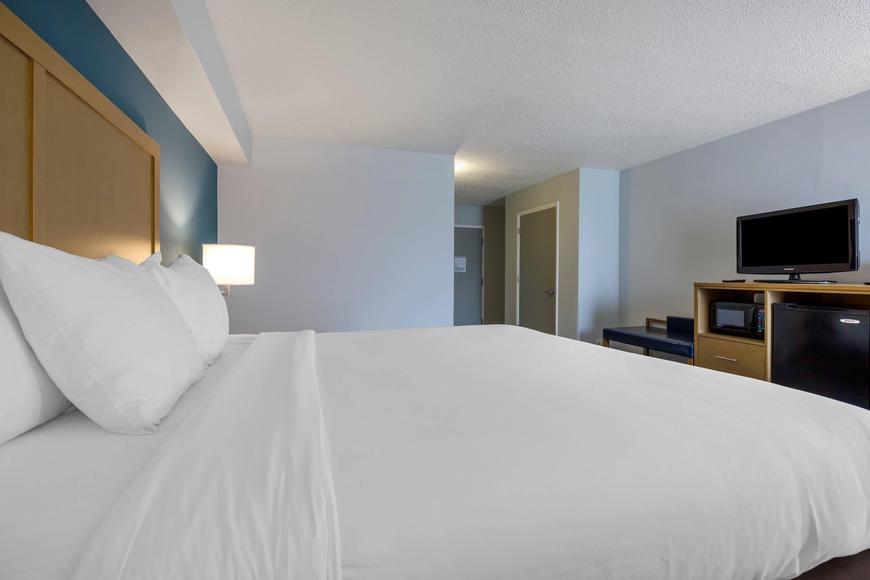 Quarto de hotel com uma cama grande, televisão em suporte de madeira, micro-ondas e frigorífico.