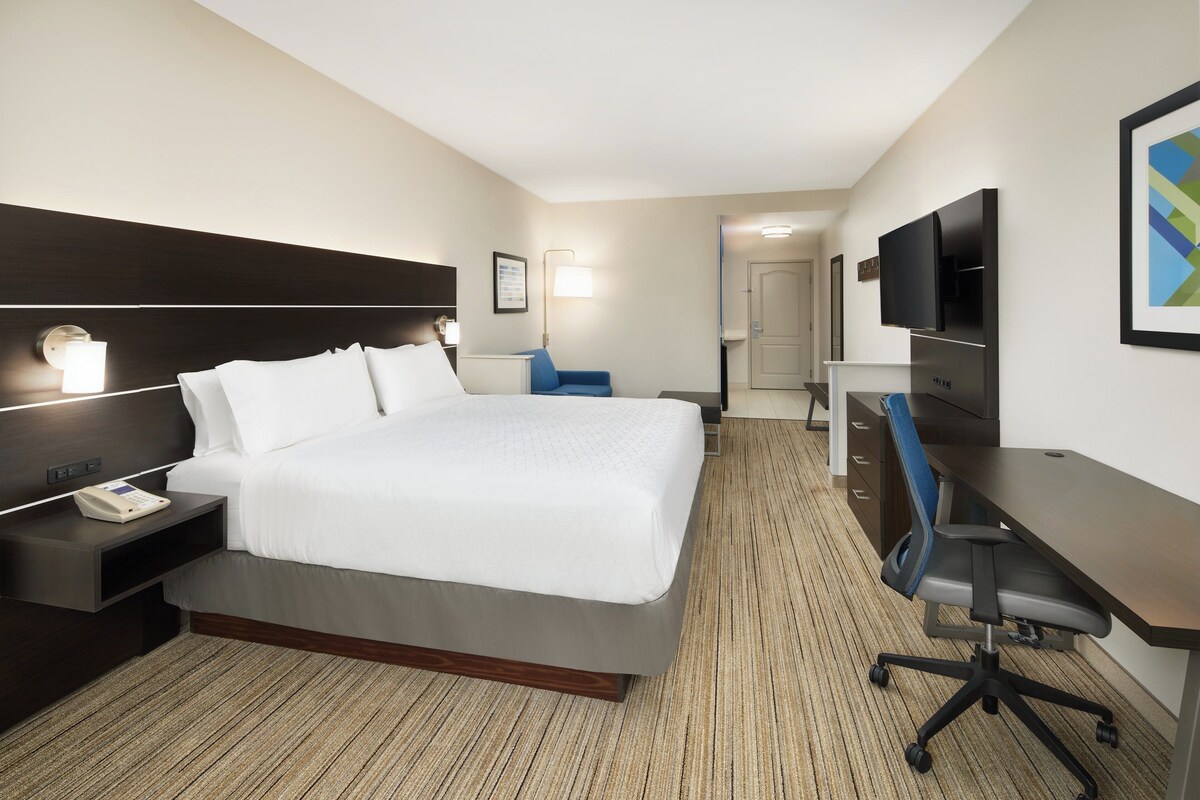 Quarto de hotel com uma cama grande, mesa de cabeceira com telefone, escrivaninha com cadeira, televisão de tela plana e TV fixada na parede.