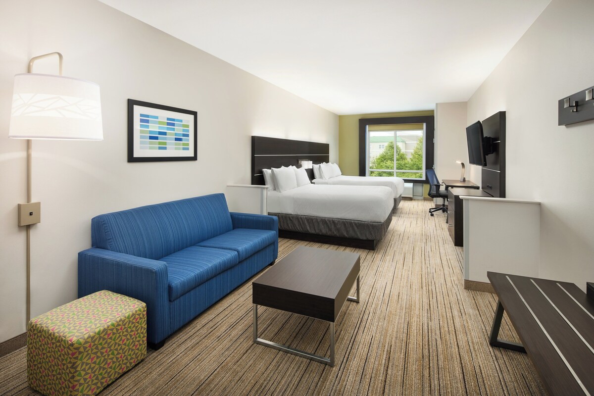 Quarto de hotel com sofá azul, cama, escrivaninha, luminária e televisão.