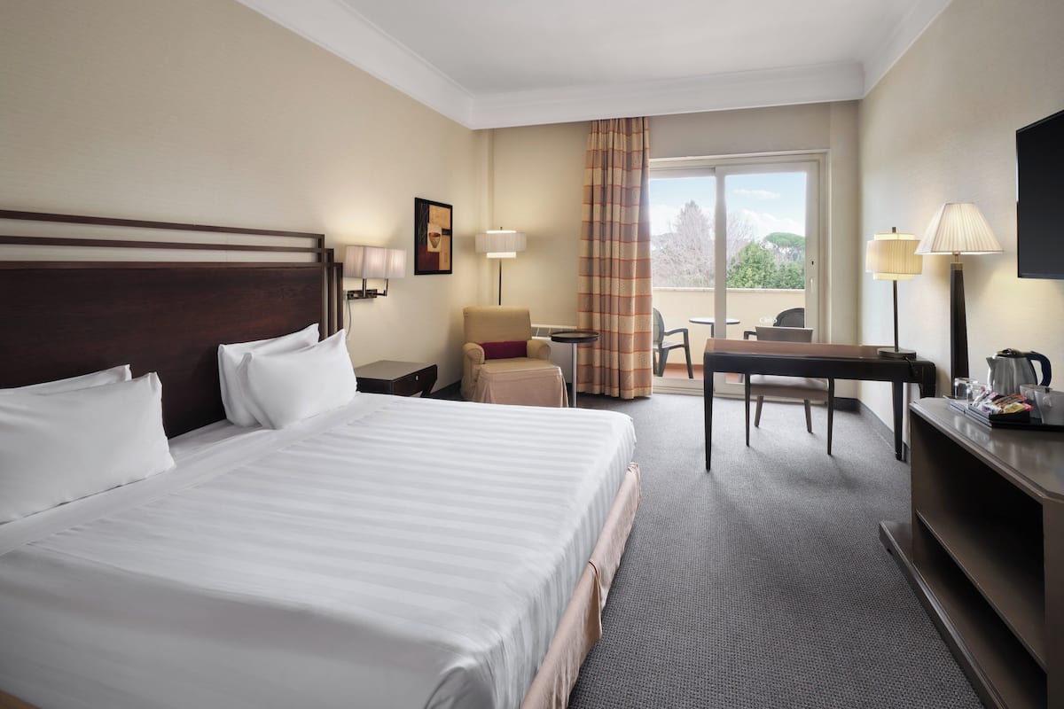 Quarto de hotel com uma cama grande, uma escrivaninha, uma cadeira, uma mesa e uma varanda com vista.