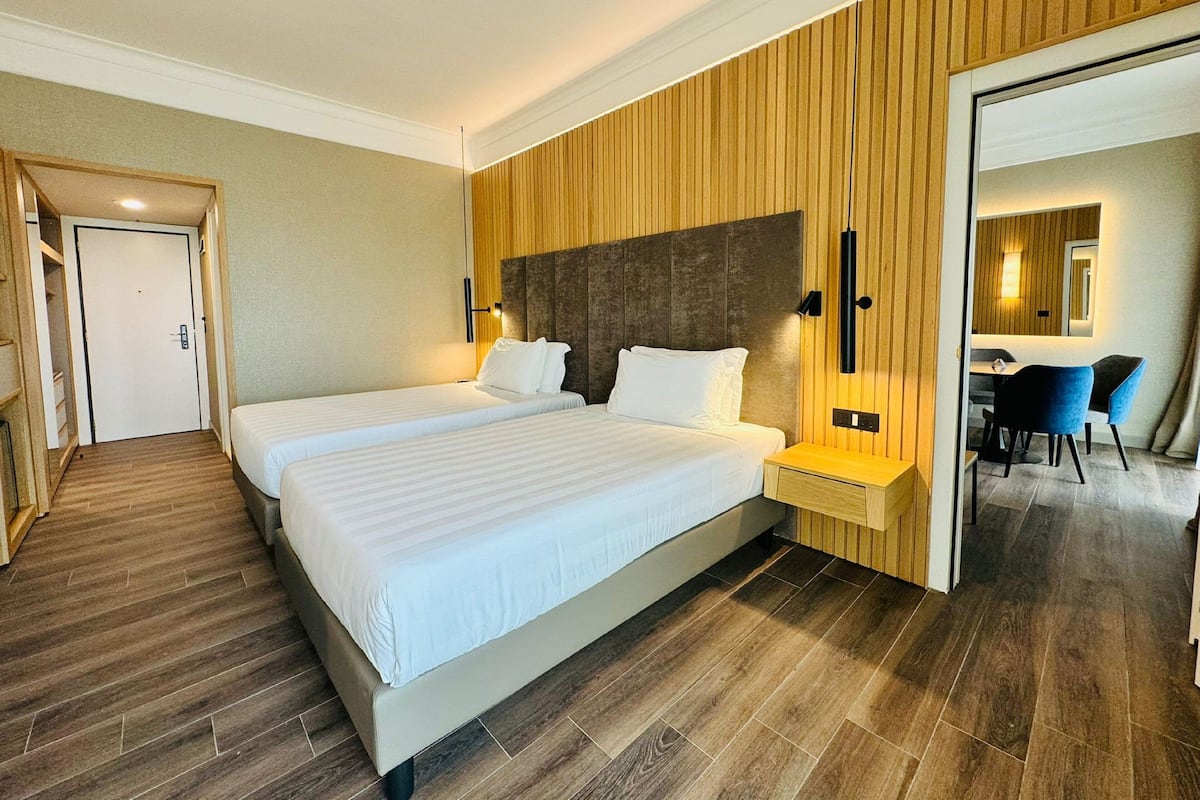 Quarto de hotel com uma cama grande, mesas de cabeceira, uma escrivaninha com cadeiras e um espelho.