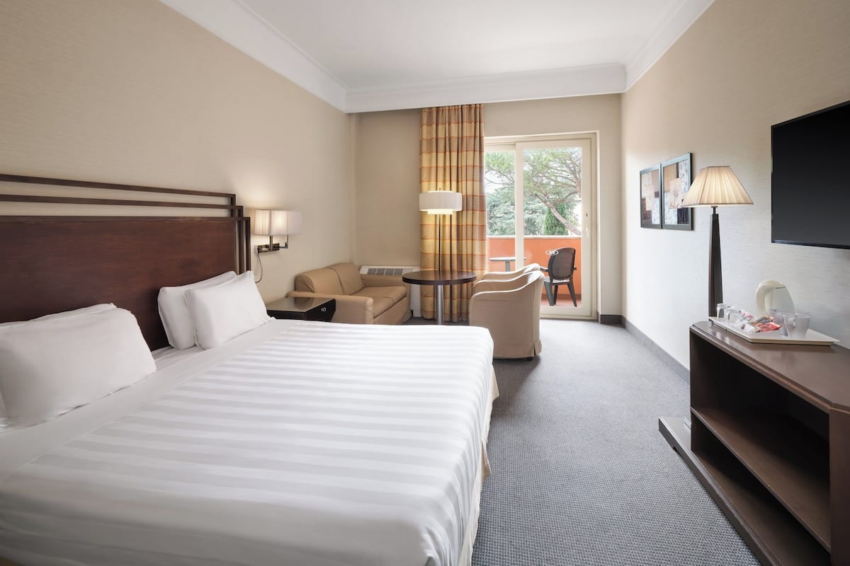 Quarto de hotel com uma cama grande, uma escrivaninha, uma cadeira, uma mesinha e uma televisão.
