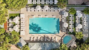Vista aérea de um resort com piscina central, várias áreas de estar com espreguiçadeiras e vegetação ao redor.