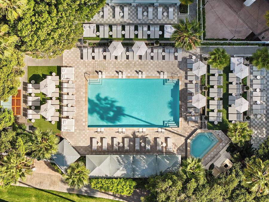 Vista aérea de um resort com piscina central, várias áreas de estar com espreguiçadeiras e vegetação ao redor.