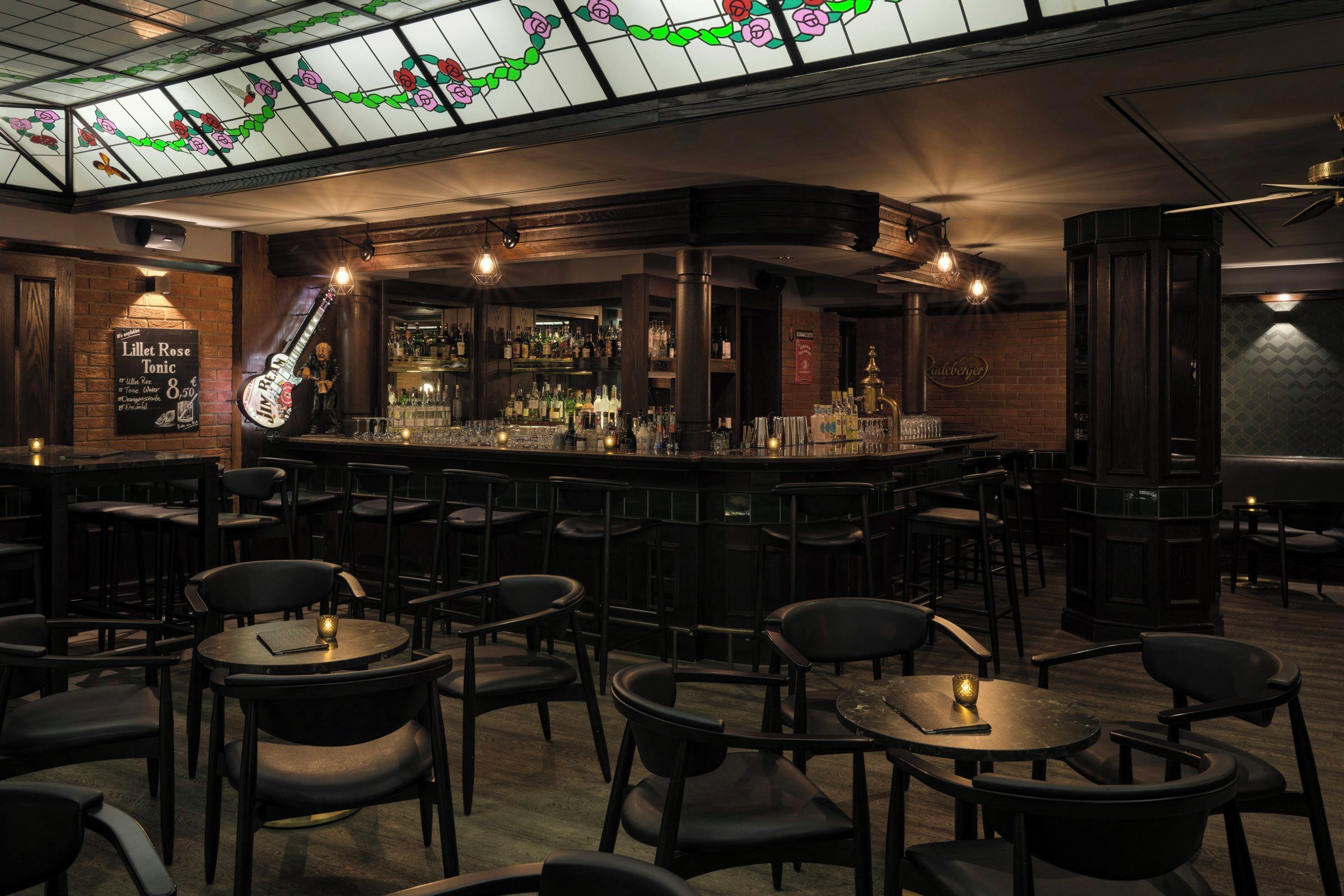 Uma área de bar com pé-direito alto, balcão de madeira e diversos arranjos de assentos, incluindo mesas e cadeiras.