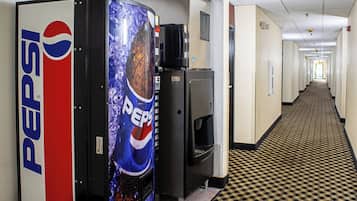 Um corredor com máquinas de venda automática, incluindo uma máquina de Pepsi, e um chão quadriculado.