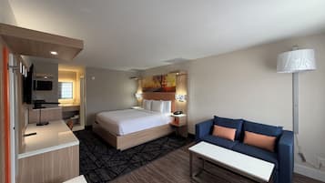 Quarto de hotel com cama, escrivaninha, sofá, televisão e um quadro na parede.