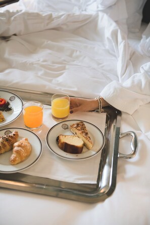 Uma bandeja com itens de café da manhã, incluindo croissants e torradas, um copo de suco de laranja e uma xícara de café, sobre uma cama.
