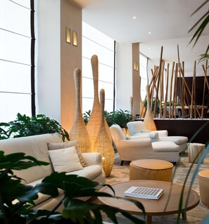 Uma área de estar moderna com sofás, uma mesa de centro redonda e luminárias altas e trançadas.
