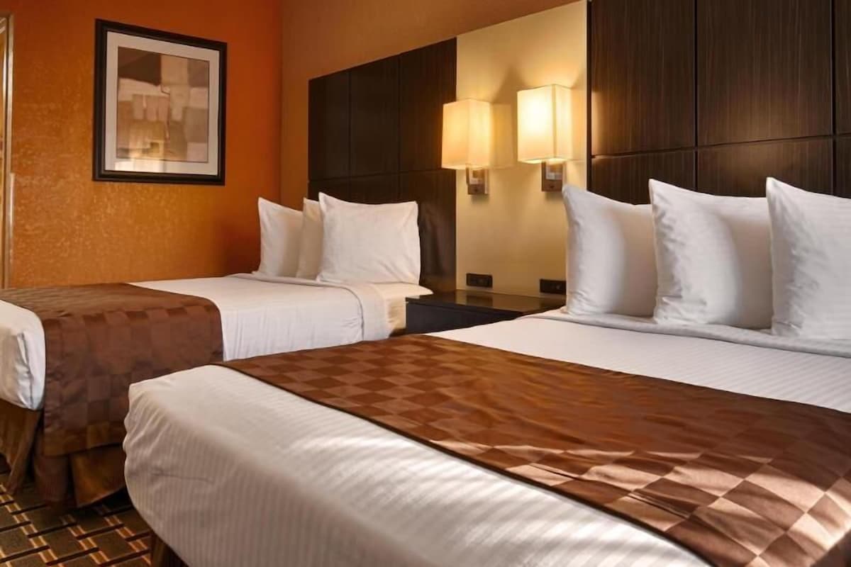 Quarto de hotel com duas camas, uma televisão grande fixada na parede e um quadro emoldurado.