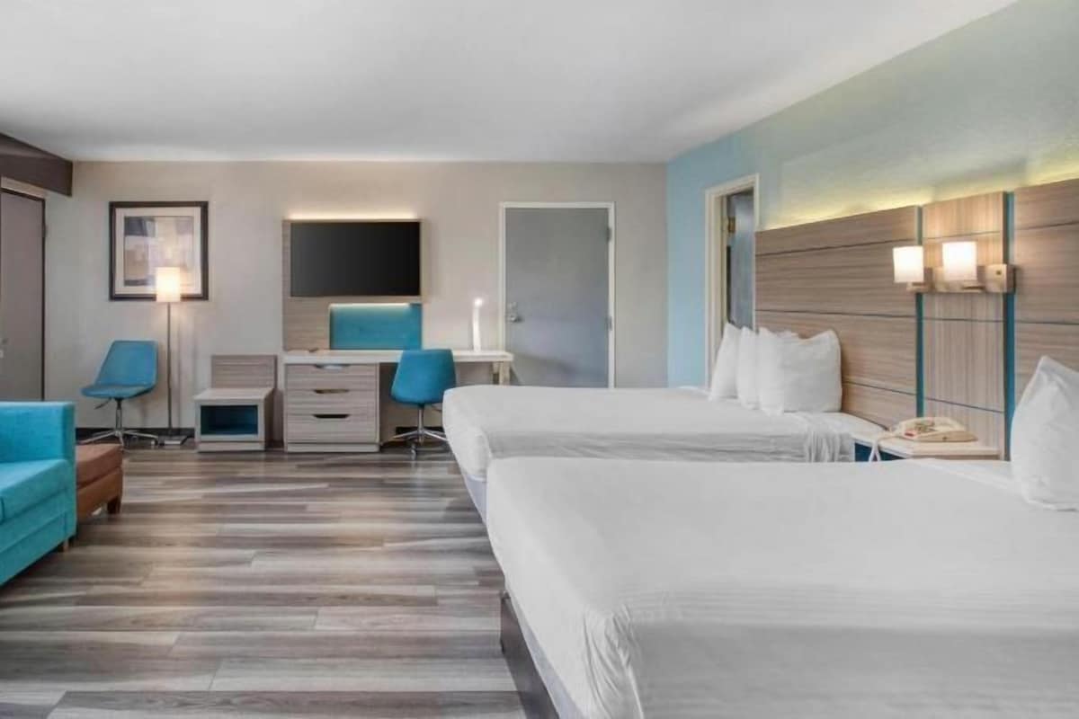 Quarto de hotel com duas camas, uma escrivaninha, uma cadeira, um sofá e uma televisão.