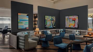 Um hall de hotel moderno com um sofá modular, poltronas azuis e arte abstrata nas paredes.