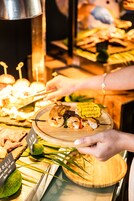 Buffet com diversos pratos, incluindo camarão, bife e espiga de milho.