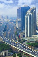 Uma movimentada autoestrada urbana com várias faixas e viadutos, cercada por edifícios altos e áreas verdes.