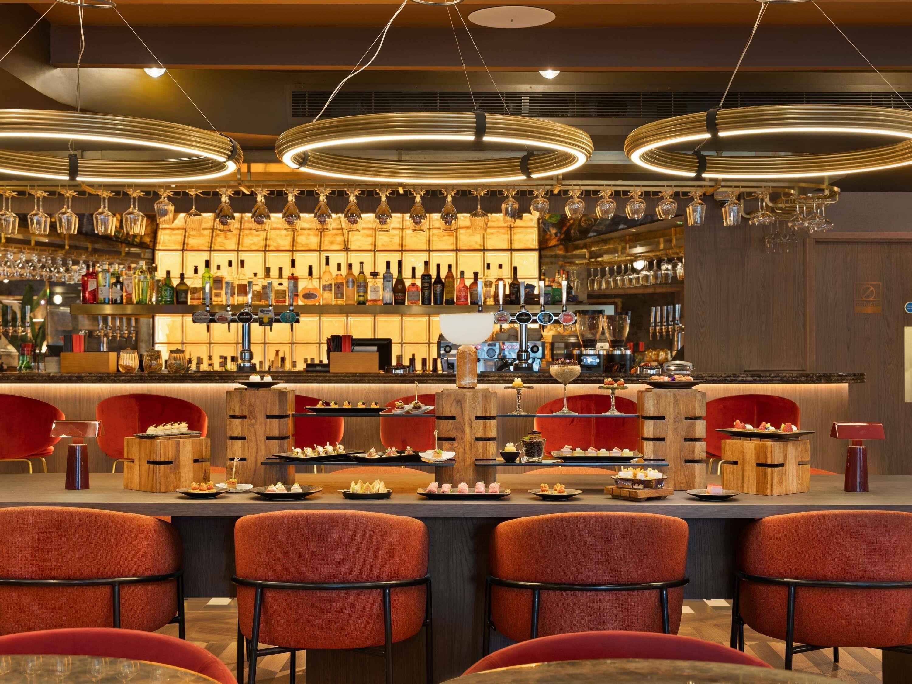 Uma área de bar com diversas opções de assento, um balcão de bar bem abastecido e uma variedade de garrafas e copos.