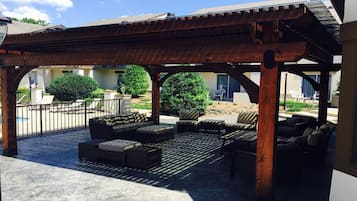 Uma área de estar coberta ao ar livre, com pérgola, mobiliário e vista para um bairro residencial.