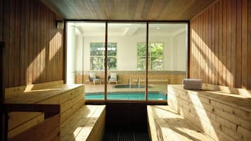 Sala de sauna com bancos de madeira, parede de vidro e vista para uma área de estar externa.