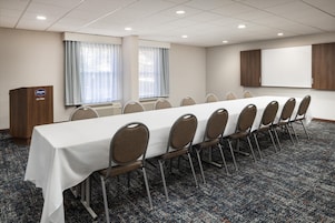 Uma sala de conferência com uma mesa grande, cadeiras, um púlpito e uma tela.