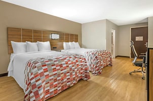 Quarto de hotel com duas camas, uma cabeceira de madeira, uma escrivaninha com cadeira e uma porta.