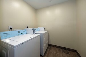 Uma lavanderia com duas máquinas de lavar e secar Whirlpool, uma tomada elétrica na parede e piso revestido com azulejos.