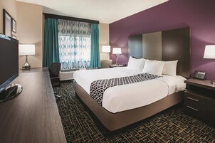 Quarto de hotel com uma cama grande, duas mesas de cabeceira com luminárias, uma escrivaninha com computador e uma televisão.