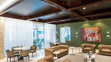 Um hall espaçoso com teto alto, área de estar com sofás e poltronas, mesa de jantar e uma grande janela com vista para o exterior.