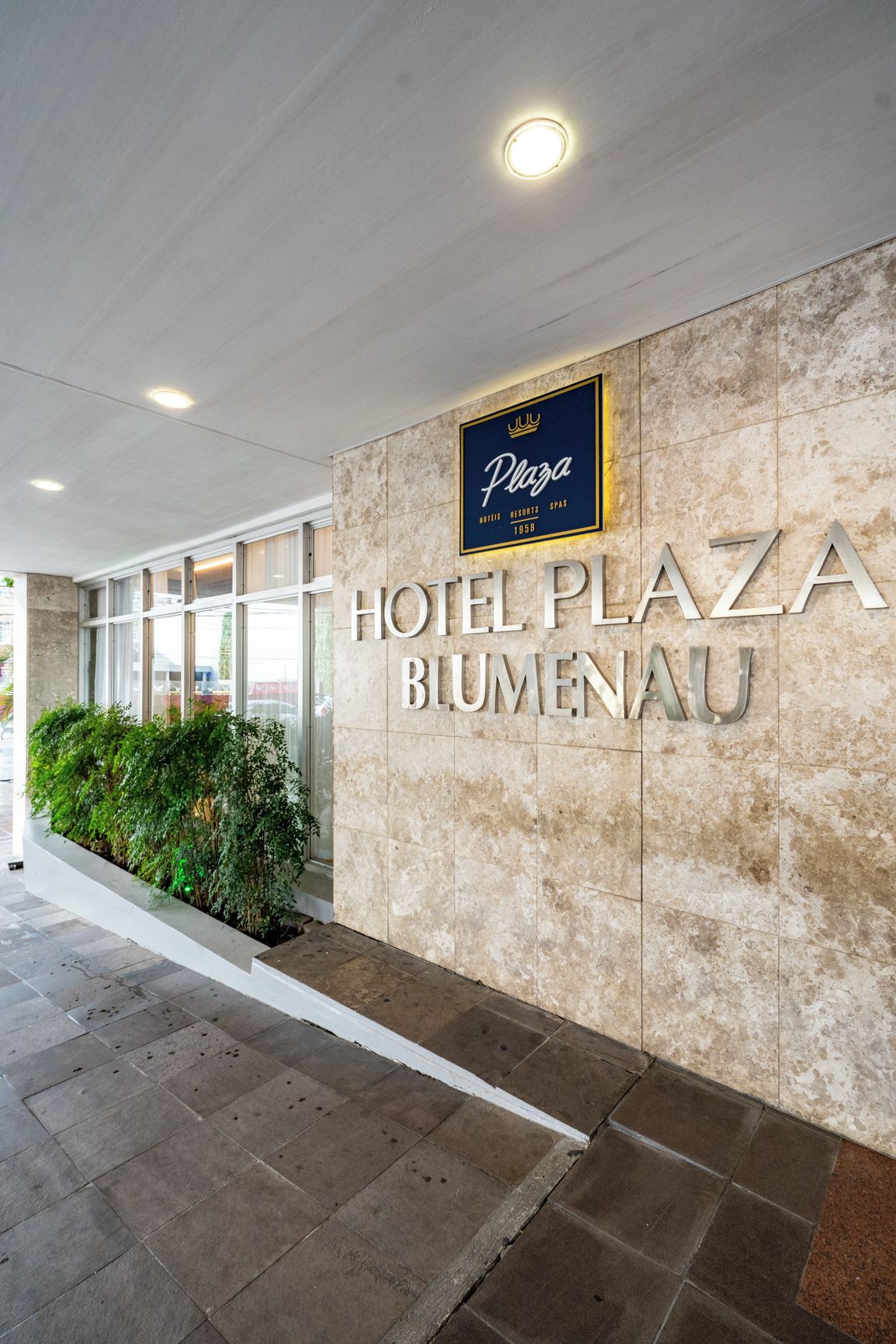 Entrada de hotel com placa indicando 'Hotel Plaza Blumenau'.