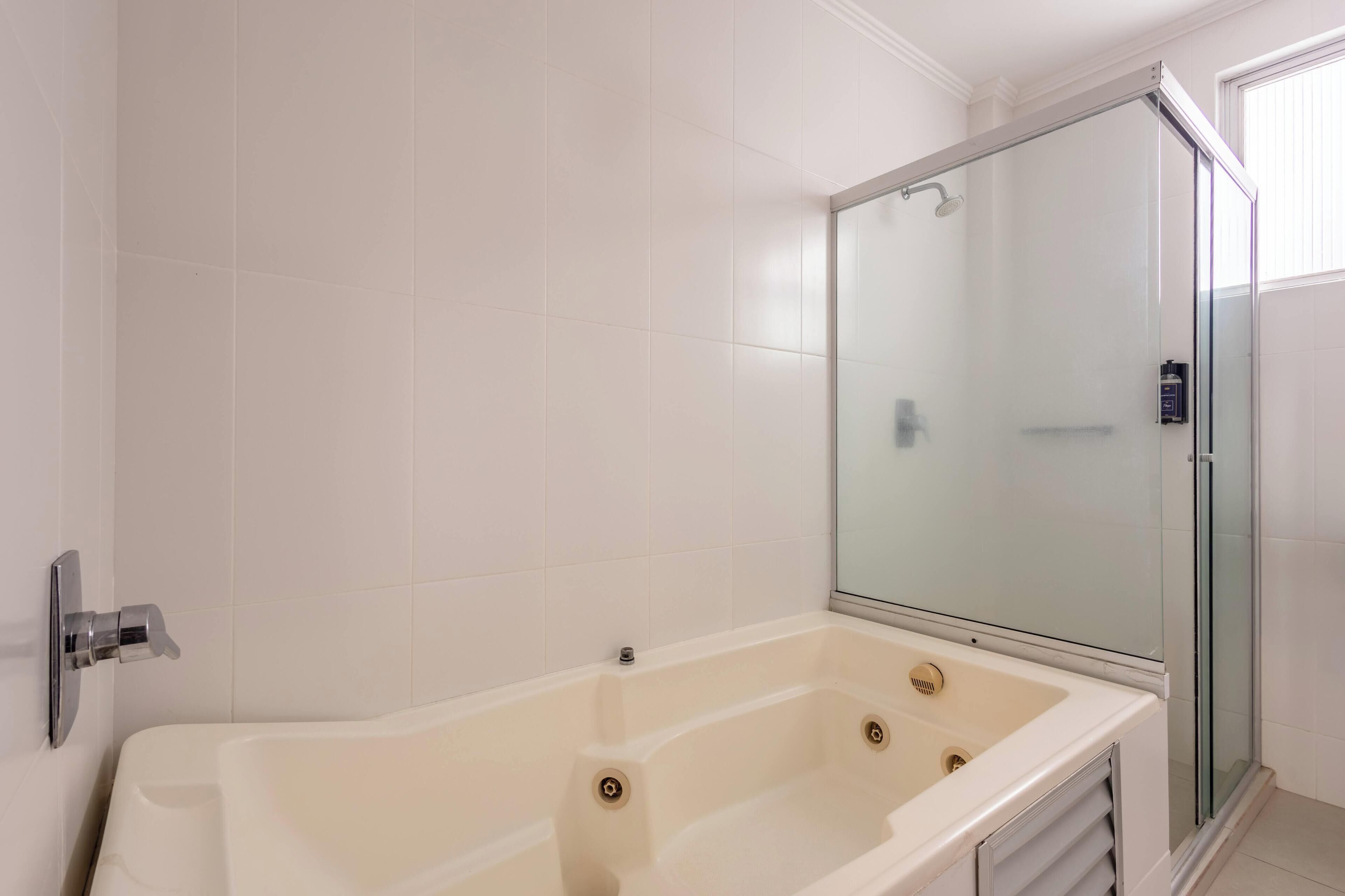 Um banheiro moderno com uma banheira grande, box de vidro e paredes com azulejos brancos.