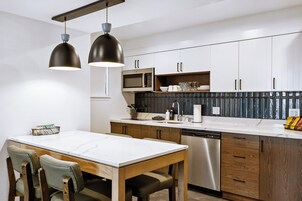 Uma cozinha moderna com armários brancos, lava-louças em aço inoxidável e bancada de mármore.