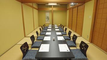 Uma sala de conferências com uma longa mesa, cadeiras e piso de tatame tradicional japonês.