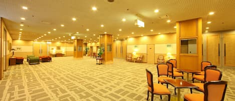 Um amplo hall de hotel com carpete estampado, várias áreas de estar e uma planta central.