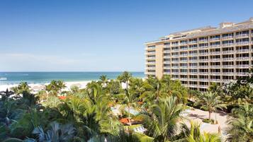 Um hotel com vista para a praia, várias varandas e uma área de piscina rodeada de palmeiras.