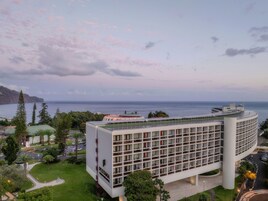 Um hotel moderno com fachada curva, várias varandas e vista para o mar.