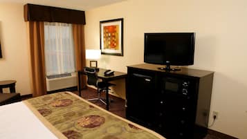 Quarto de hotel com cama, escrivaninha com computador, televisão e ar-condicionado fixado na parede.