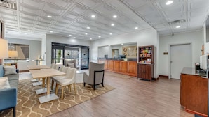 Uma sala ampla com mesa de jantar, cadeiras e sofá. Há também uma cozinha com armários de madeira e bancada.