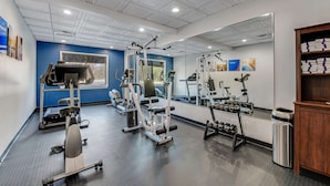 Uma academia com diversos equipamentos de exercício, um espelho grande e uma janela.
