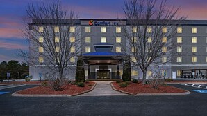 Um hotel Comfort Inn com fachada moderna, entrada coberta e acesso por uma alameda arborizada.
