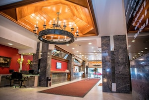 Um saguão de hotel com teto de madeira, um candelabro, um balcão de recepção e uma parede vermelha com uma moldura.