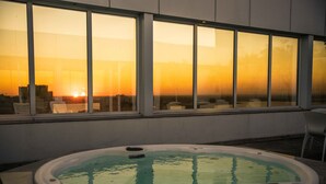 Uma banheira de hidromassagem com vista para um pôr do sol através de grandes janelas.