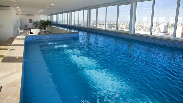 Uma piscina interna com vista para a cidade, uma área de estar com cadeiras e um vaso de planta.