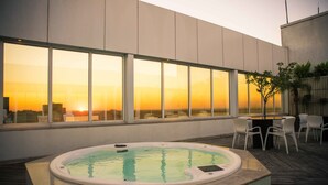 Terraço no telhado com hidromassagem, mobiliário para área externa e grandes janelas com vista para o pôr do sol.