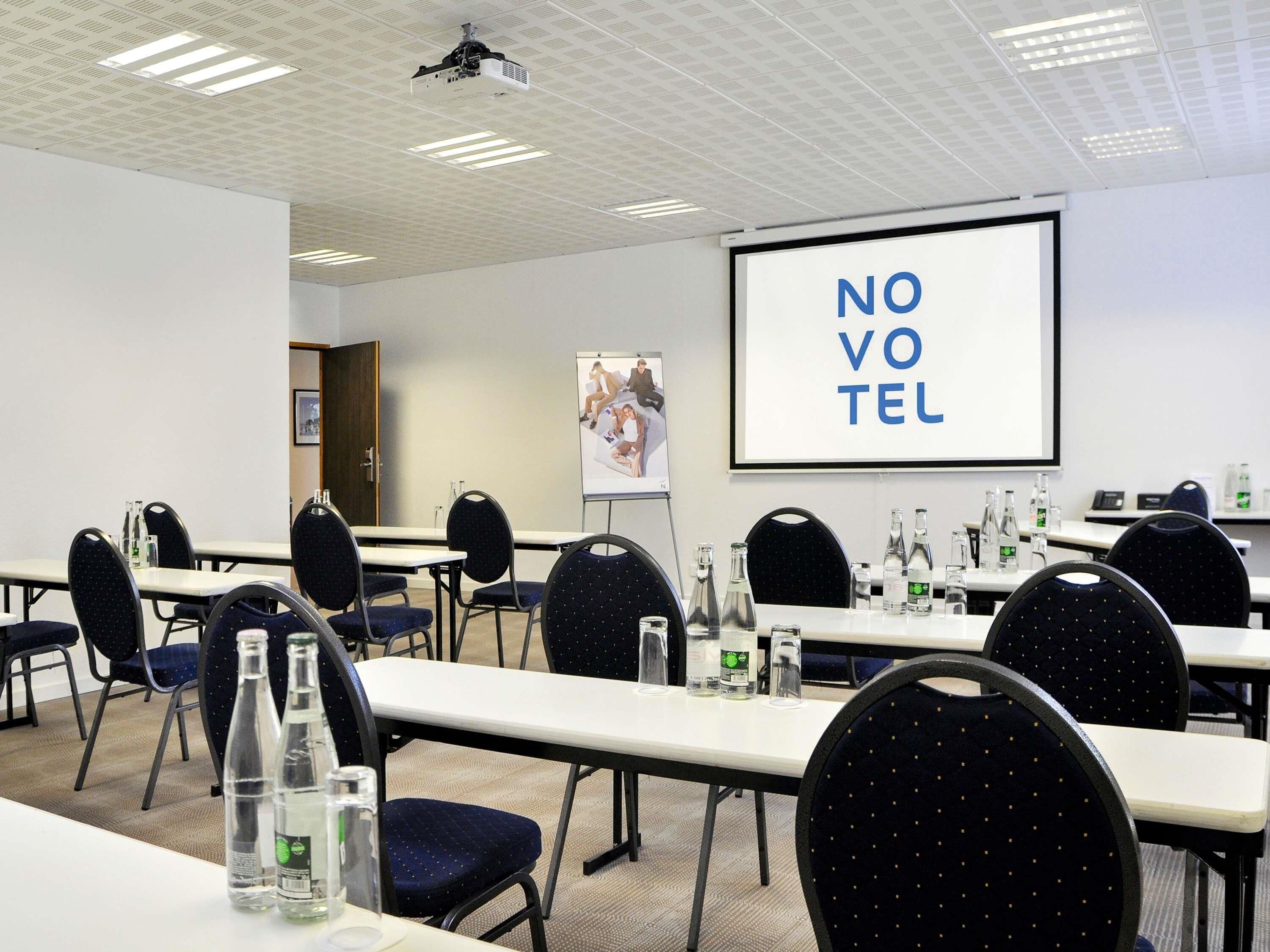 Uma sala de conferência com mesas, cadeiras, um projetor e uma tela exibindo 'NO VOTEL'.