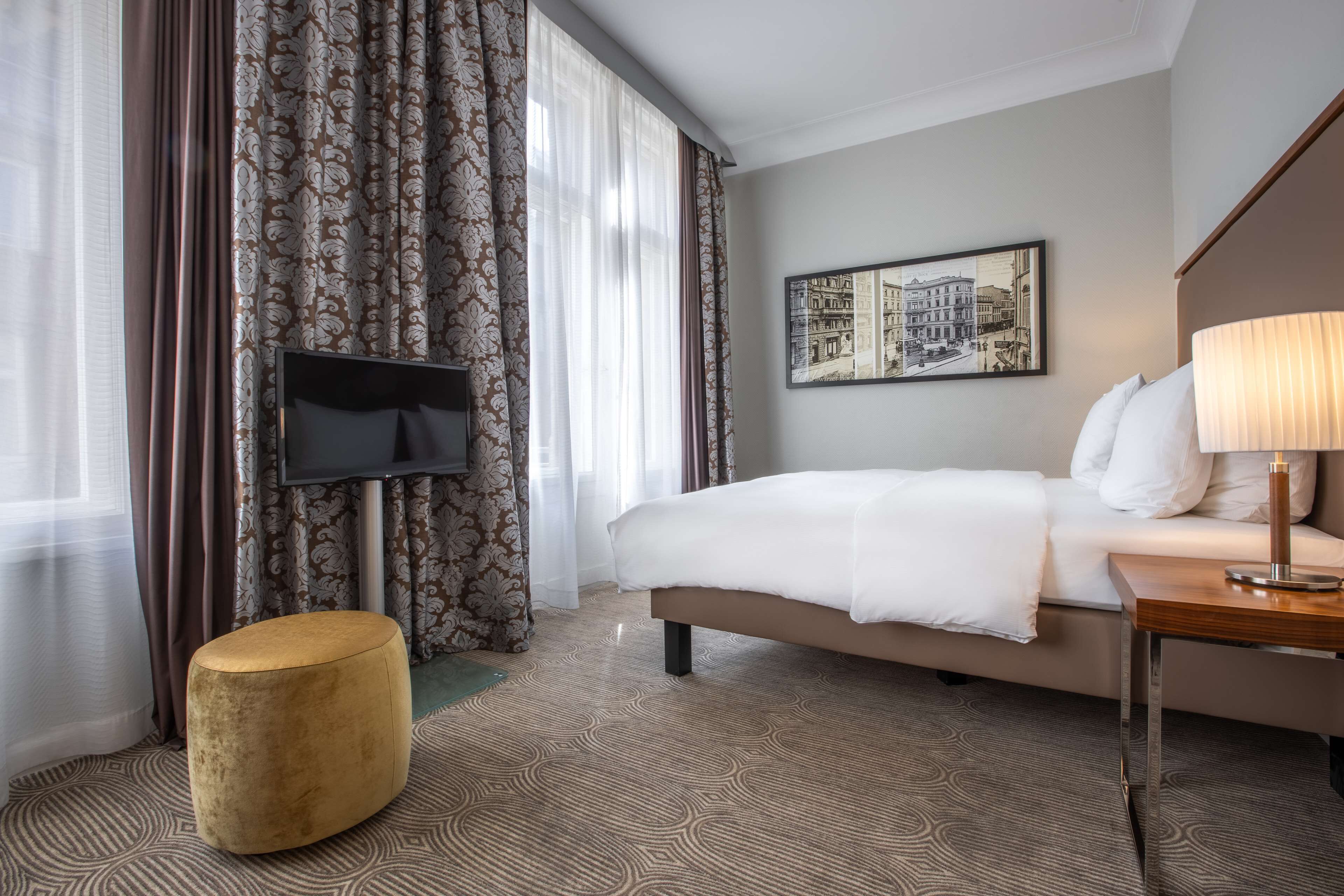 Quarto de hotel com cama, televisão, luminária e tapete estampado.