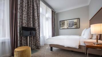 Quarto de hotel com cama, televisão, luminária e tapete estampado.