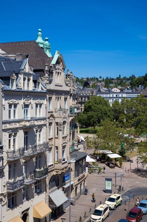 Um edifício histórico com arquitetura elaborada, uma rua com carros estacionados e um céu azul claro.