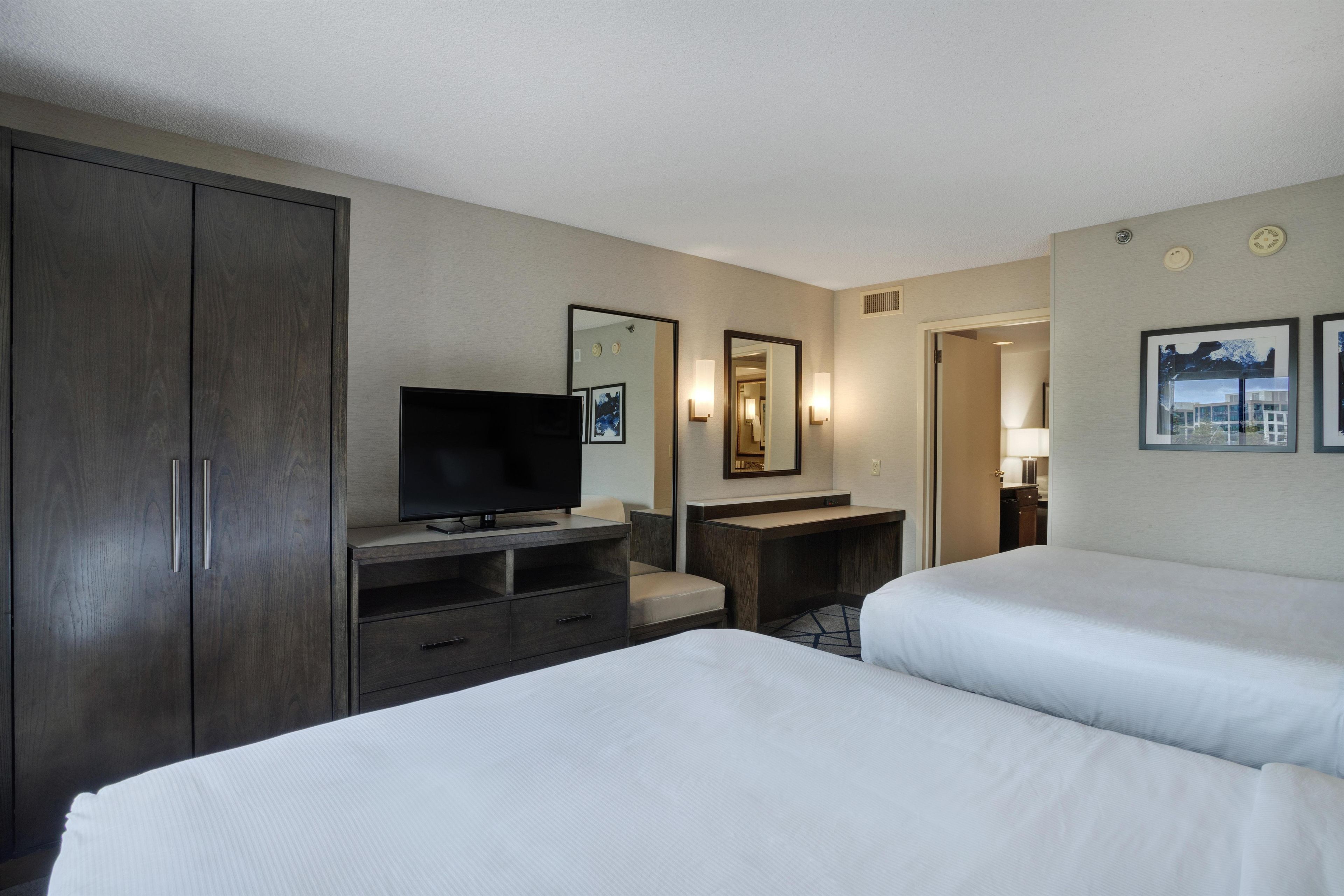 Quarto de hotel com duas camas, televisão, escrivaninha e guarda-roupa.