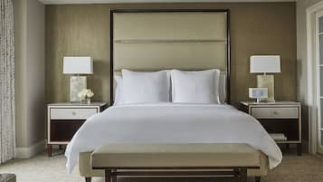 Quarto de hotel com uma cama grande, duas mesas de cabeceira com abajures, um banco e vista para o exterior.